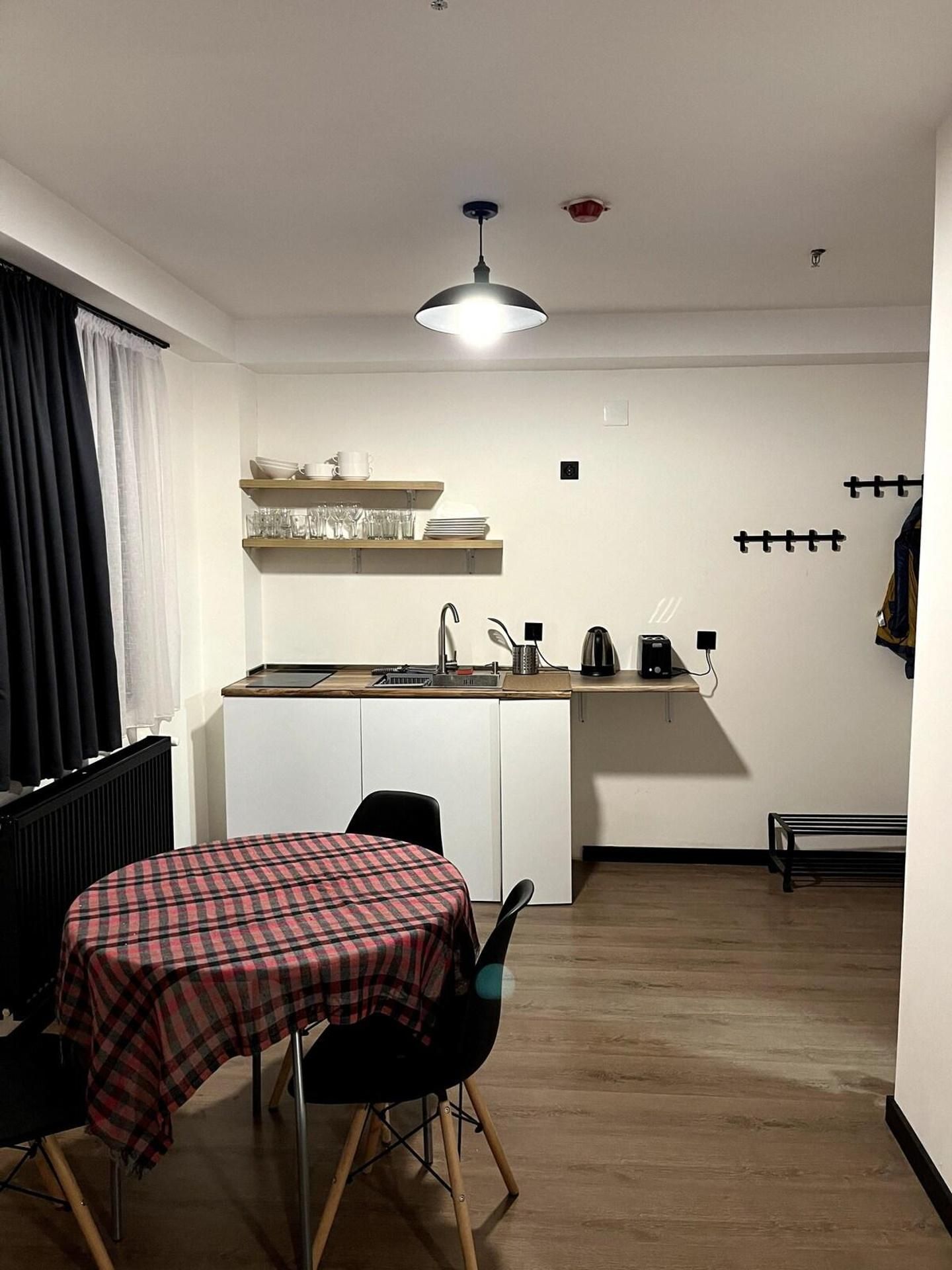 Cozinha compacta com área de jantar, mesa com toalha xadrez e uma cadeira.