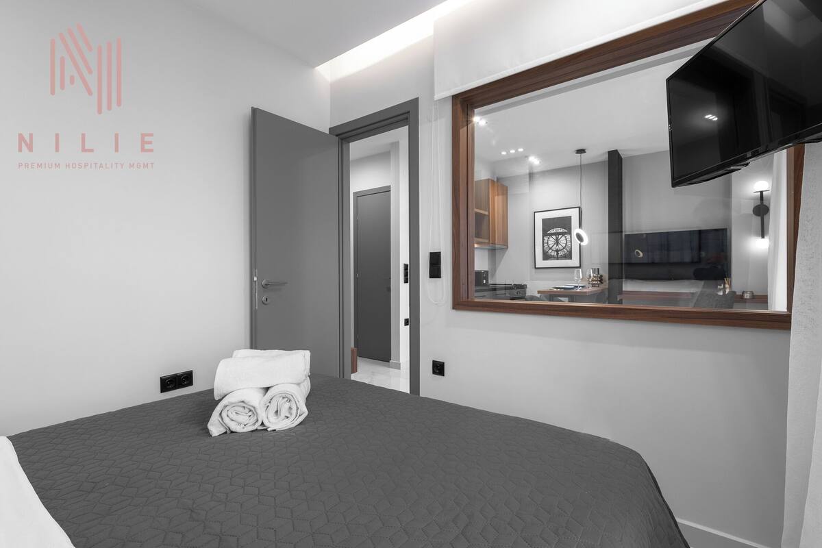 Quarto de hotel moderno com uma cama grande, uma toalha bem dobrada, uma TV de tela plana na parede e um espelho refletindo o interior do quarto.