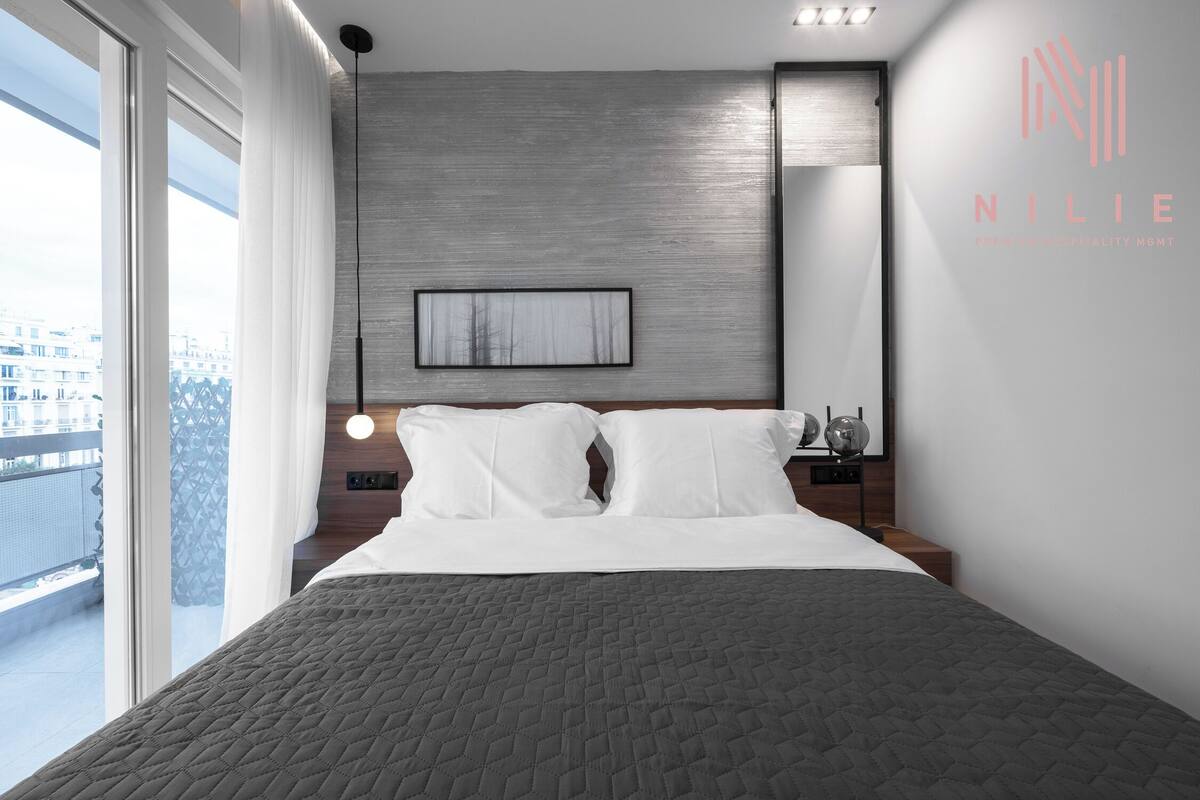 Quarto de hotel moderno com uma cama grande, vista da cidade e uma obra de arte emoldurada na parede.