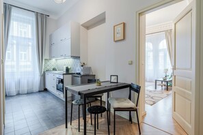 Cozinha compacta com eletrodomésticos modernos, sala de jantar com mesa e cadeiras, e vista para o exterior através de uma janela.