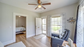 Ampla sala de estar com ventilador de teto, sofá, mesa de centro e vista para o exterior.