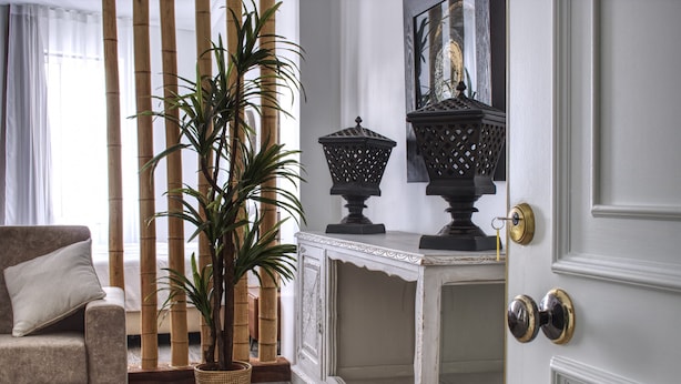 Quarto com sofá, planta em vaso, mesa de apoio com objetos decorativos e porta com puxador de latão.