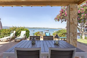 Uma área de estar coberta ao ar livre, com mesa e cadeiras, com vista para um corpo de água com barcos.
