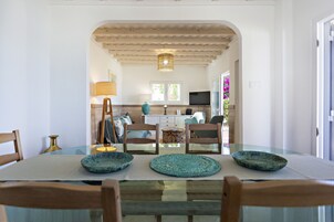 Uma sala de jantar com mesa de vidro, cadeiras de madeira e cozinha ao fundo.