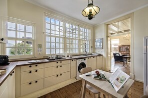 Uma cozinha com grandes janelas, máquina de lavar e área de refeições com mesa e cadeiras.