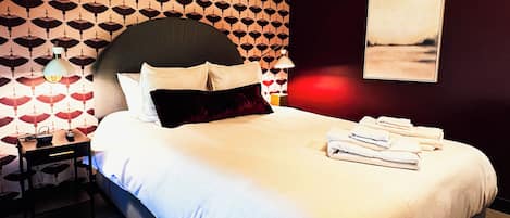 Quarto de hotel com uma cama grande, mesa de cabeceira, abajur e parede com papel de parede estampado.