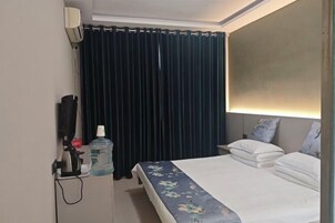 Quarto de hotel com uma cama, um grande dispensador de água, um telefone e uma cortina.
