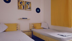 Quarto com duas camas de madeira, cada uma com travesseiro e uma pequena mesa de cabeceira. Duas imagens emolduradas na parede e uma estante com um livro.