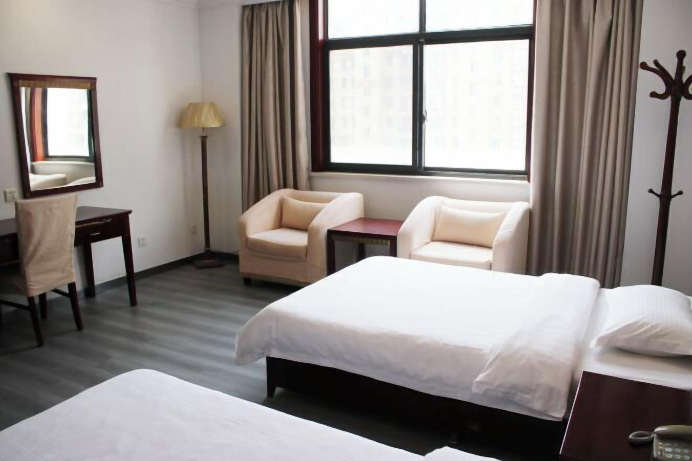 Quarto de hotel com duas camas, uma escrivaninha, uma cadeira, um abajur e uma janela com cortinas.