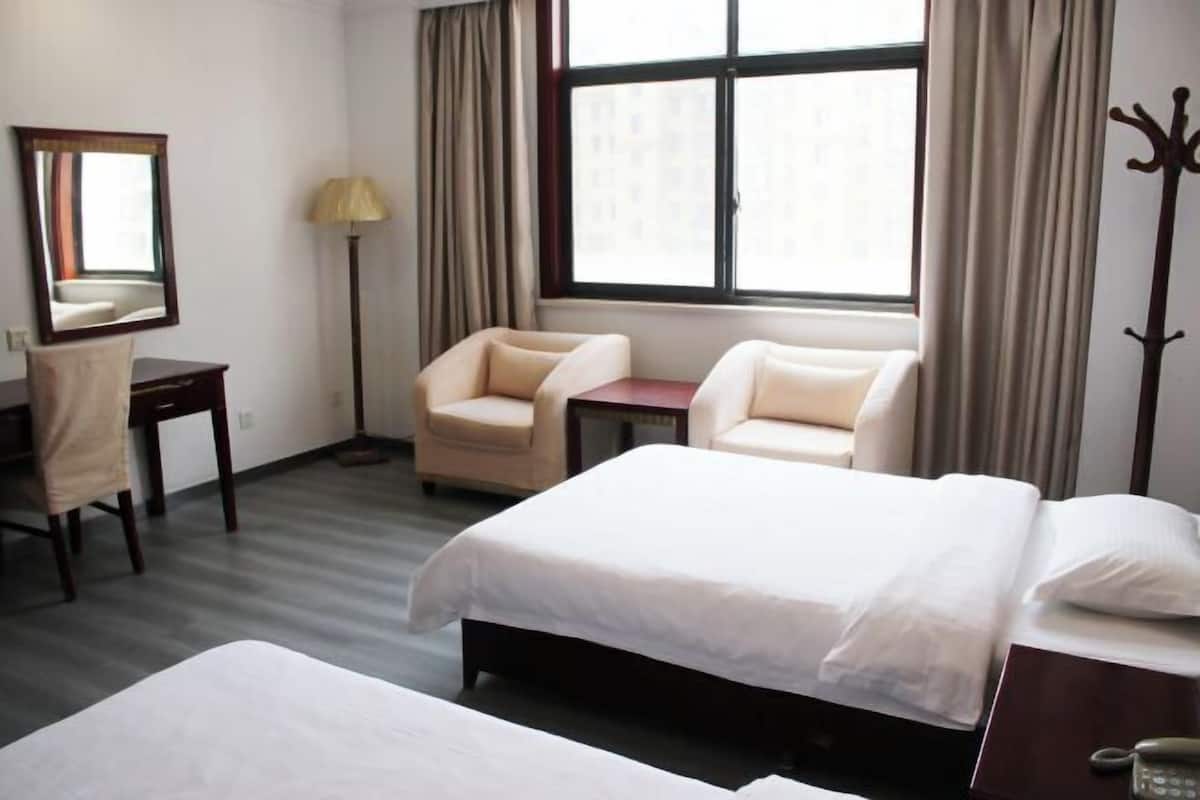 Quarto de hotel com duas camas, uma escrivaninha, uma cadeira, um abajur e uma janela com cortinas.