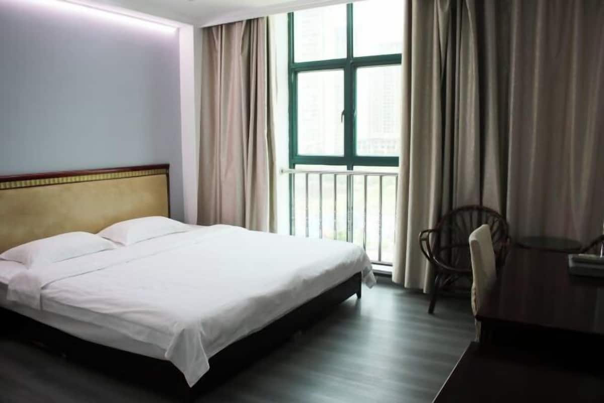 Quarto de hotel com cama, uma cadeira, escrivaninha e janela com cortinas.