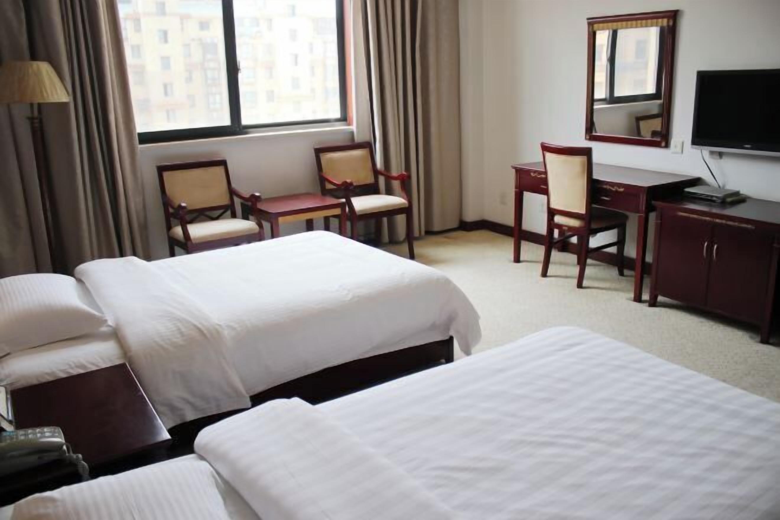 Quarto de hotel com duas camas, uma escrivaninha, uma cadeira, uma televisão e uma janela com cortinas.