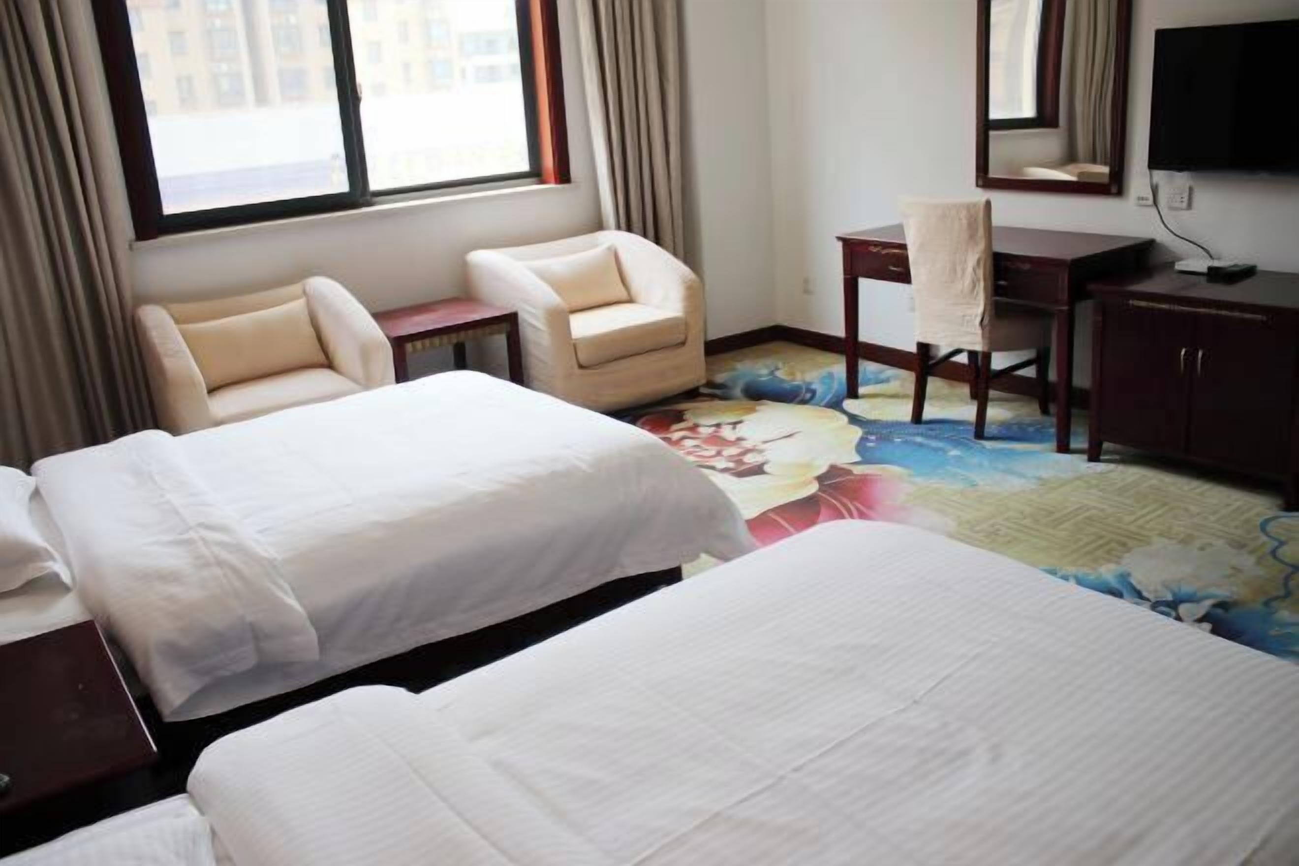 Quarto de hotel com duas camas, uma mesa, uma cadeira, uma televisão e uma janela.
