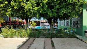 Área de piscina com piscina cercada, rodeada por árvores e um edifício verde.