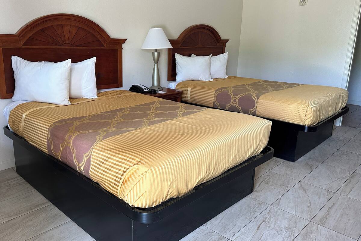 Quarto de hotel com duas camas, cada uma com cabeceira de madeira, mesa de cabeceira com abajur e uma cadeira.