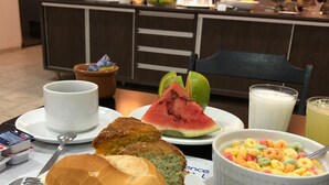Mesa posta para o café da manhã, com sanduíche, melancia, cereal, leite e uma xícara.