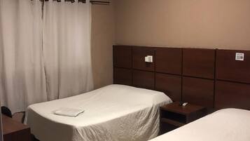 Quarto de hotel com duas camas de solteiro, cabeceira de madeira, mesa de cabeceira com telefone e ar condicionado.