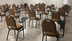Uma sala de conferências com fileiras de cadeiras, mesas, um quadro branco e um projetor.