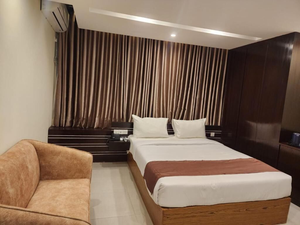 Quarto de hotel moderno com uma cama grande, um sofá, um guarda-roupa de madeira e um painel de cortinas.