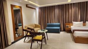 Quarto de hotel com cama, sofá, cadeira, mesa pequena e espelho.