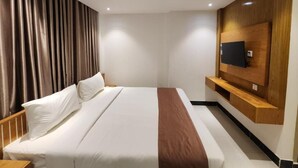 Quarto de hotel moderno com uma cama grande, cabeceira de madeira, televisão fixada na parede e cortina à esquerda.