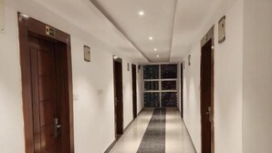Corredor de hotel comprido e estreito, com portas de madeira à esquerda e uma faixa central de azulejos escuros.