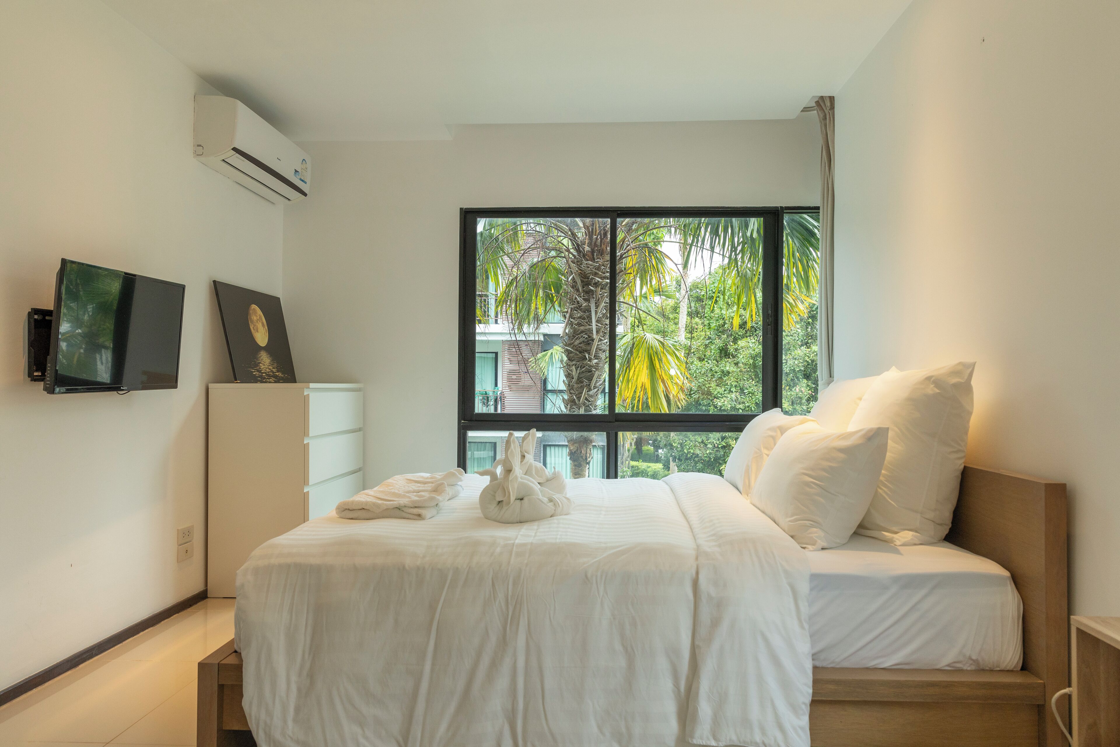 Quarto de hotel moderno com uma cama grande, uma televisão e uma janela com vista para palmeiras.