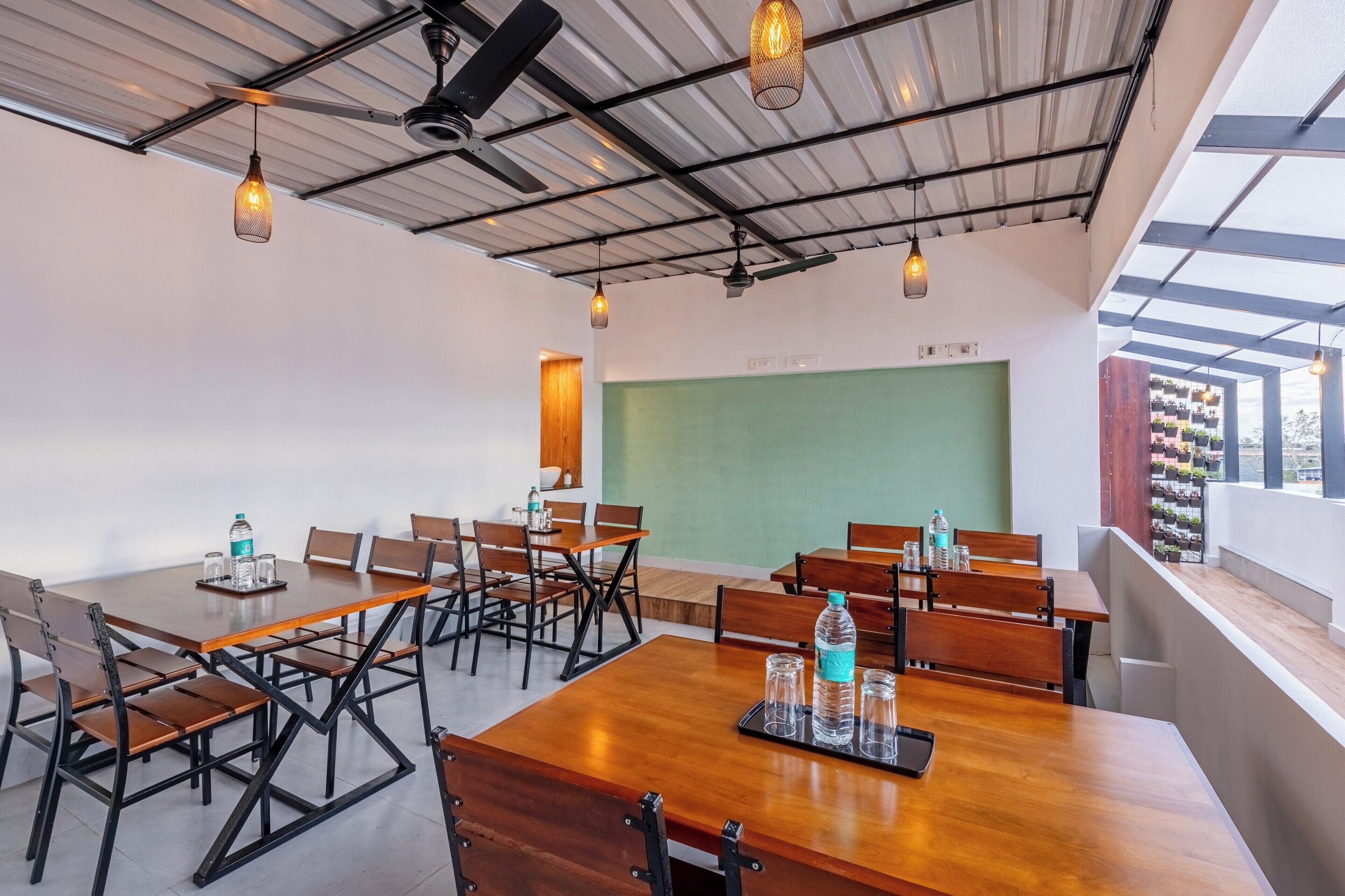 Sala de conferência com mesas e cadeiras de madeira, ventiladores de teto e luminárias pendentes.