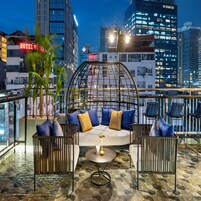 Um lounge no terraço com área de estar sob uma cúpula de vidro, uma planta em vaso e vista para o horizonte da cidade ao entardecer.