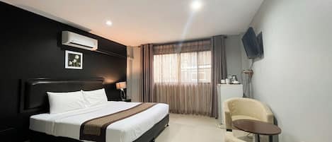 Quarto de hotel com cama, poltrona, televisão e janela com cortinas.