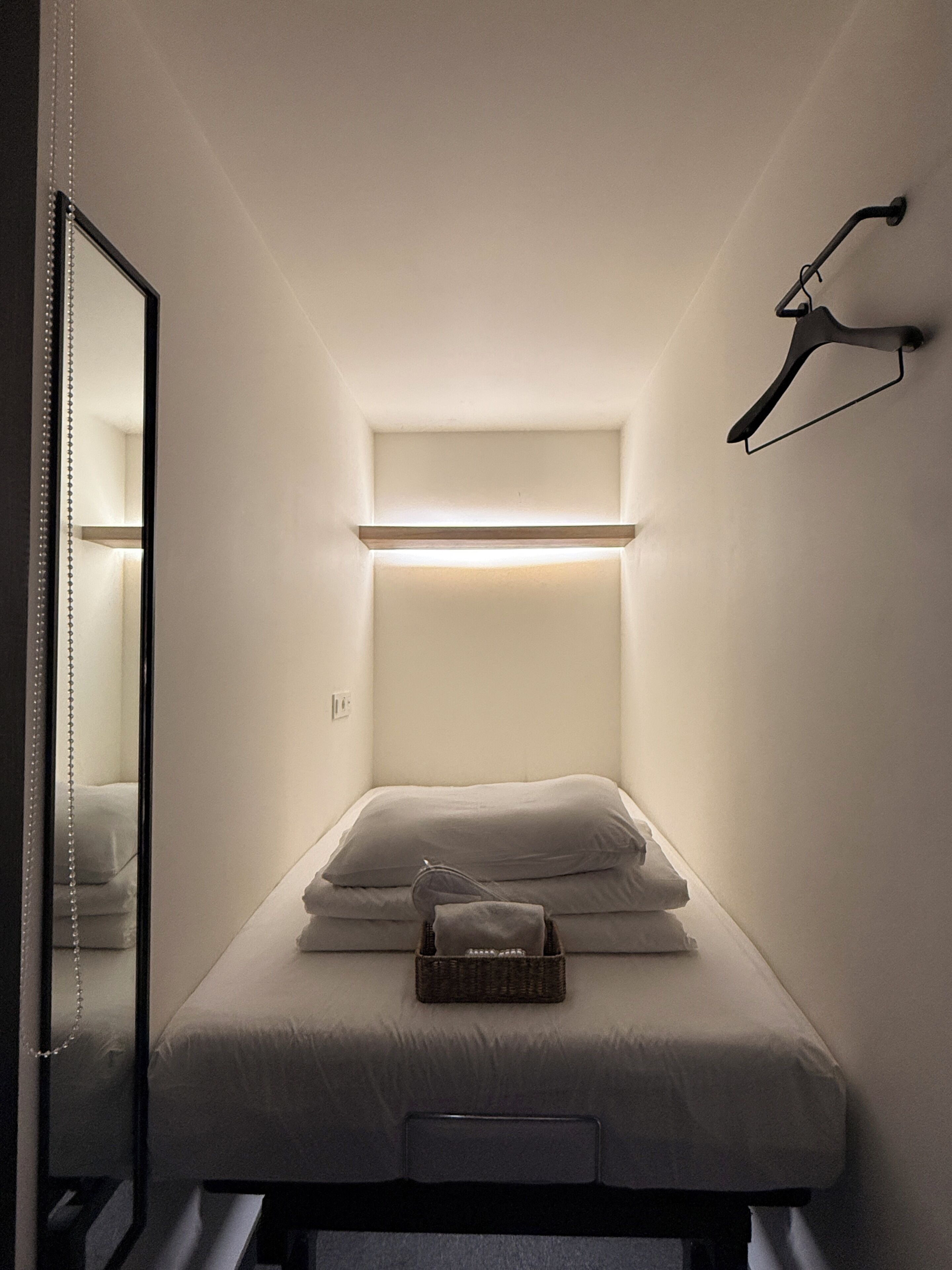 Quarto compacto com cama, luminária pendente e espelho.