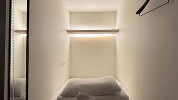 Quarto compacto com cama, luminária pendente e espelho.