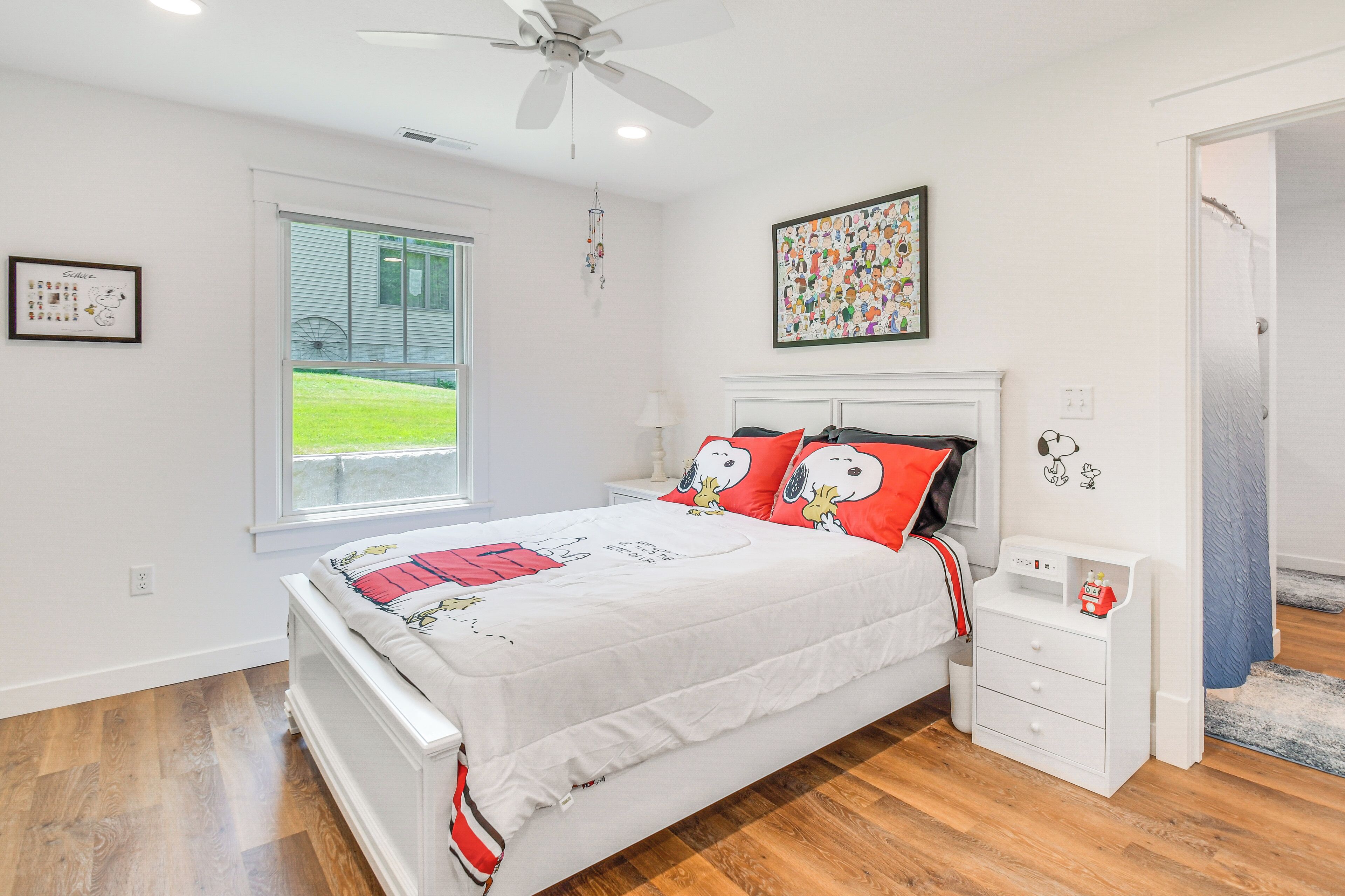 Um quarto com cama, mesa de cabeceira, ventilador de teto, janela e porta.