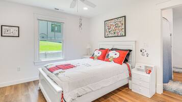 Um quarto com cama, mesa de cabeceira, ventilador de teto, janela e porta.