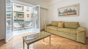 Uma sala de estar com sofá, mesa de centro de vidro e um quadro na parede.