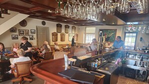 Uma área de bar com móveis de madeira, balcão e copos pendurados.