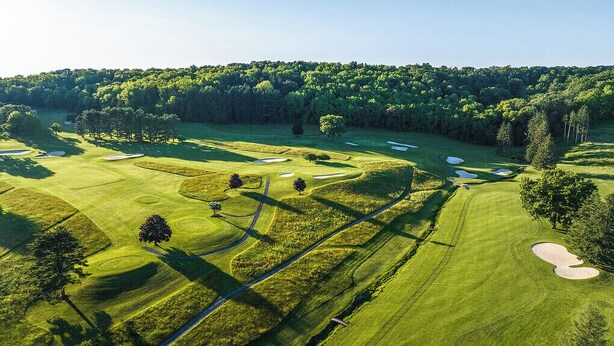 Vista aérea de um campo de golfe com vários bunkers, árvores e um céu claro.
