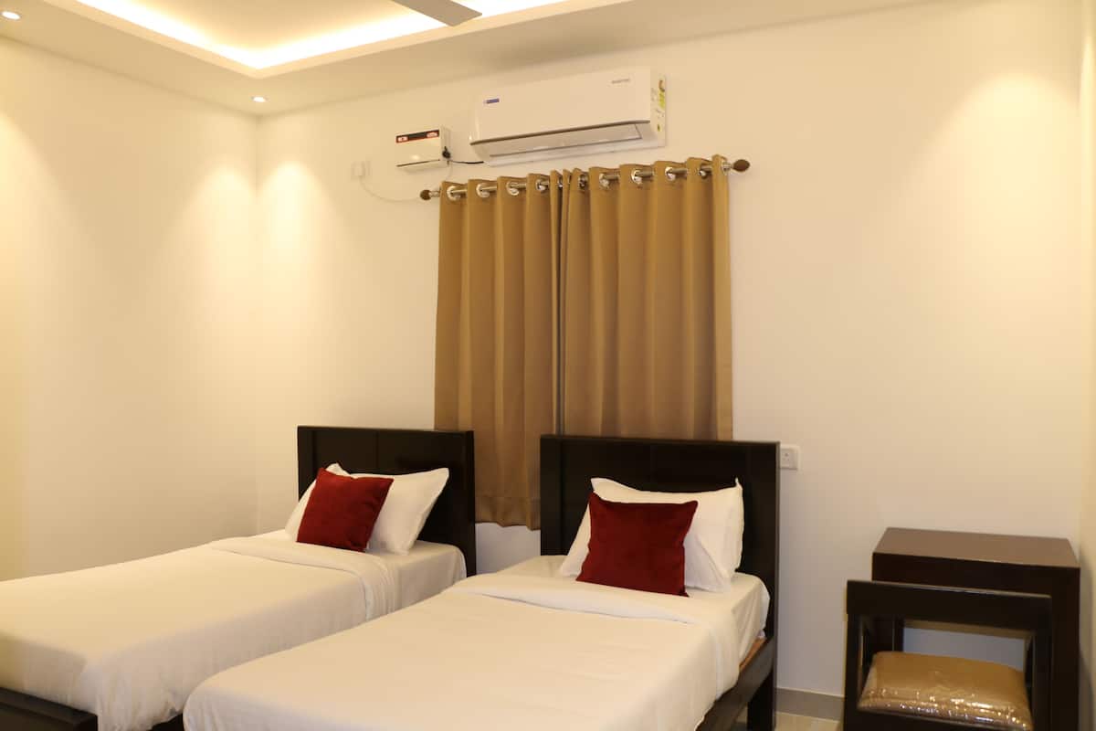Quarto de hotel com duas camas de solteiro, uma mesinha e um aparelho de ar condicionado na parede.