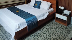 Quarto de hotel com cama de madeira, um quadro na parede, ventoinha no teto e unidade de ar condicionado.