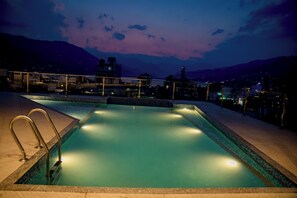 Piscina com vista para montanhas e para a cidade ao entardecer.