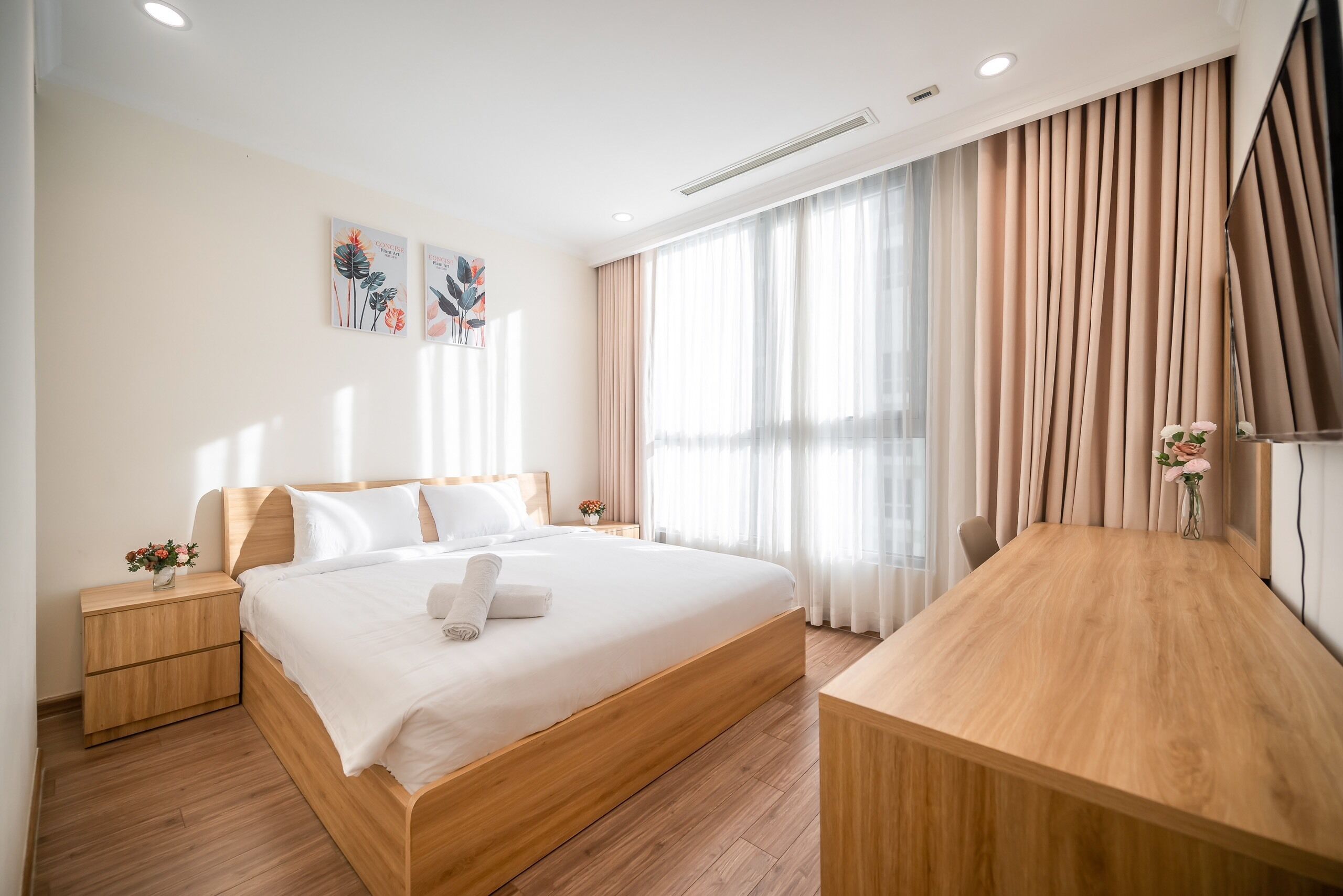 Quarto de hotel moderno com cama e escrivaninha de madeira, e uma janela grande com cortinas.