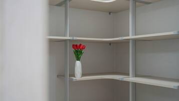Uma estante branca e vazia com um vaso branco contendo flores vermelhas em uma das prateleiras.