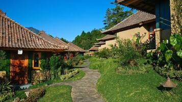 Uma trilha serpenteia por uma aldeia tradicional, com construções de palha e muita vegetação.