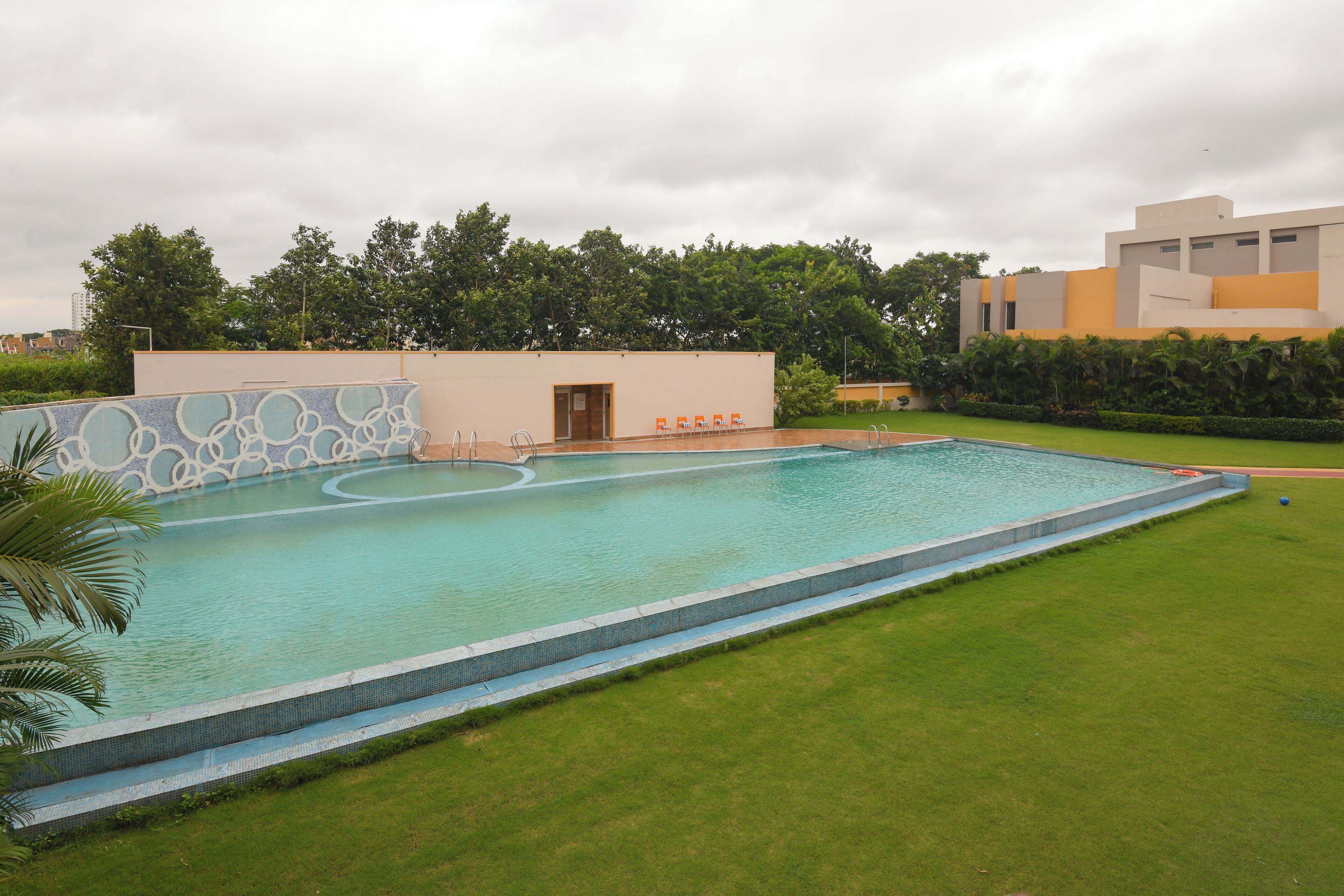 Uma piscina com design geométrico em azulejos, rodeada por um relvado bem cuidado e um edifício com fachada moderna.