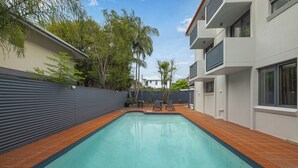 Piscina retangular com borda ladrilhada, rodeada por um deck de tijolos e uma cerca de metal.