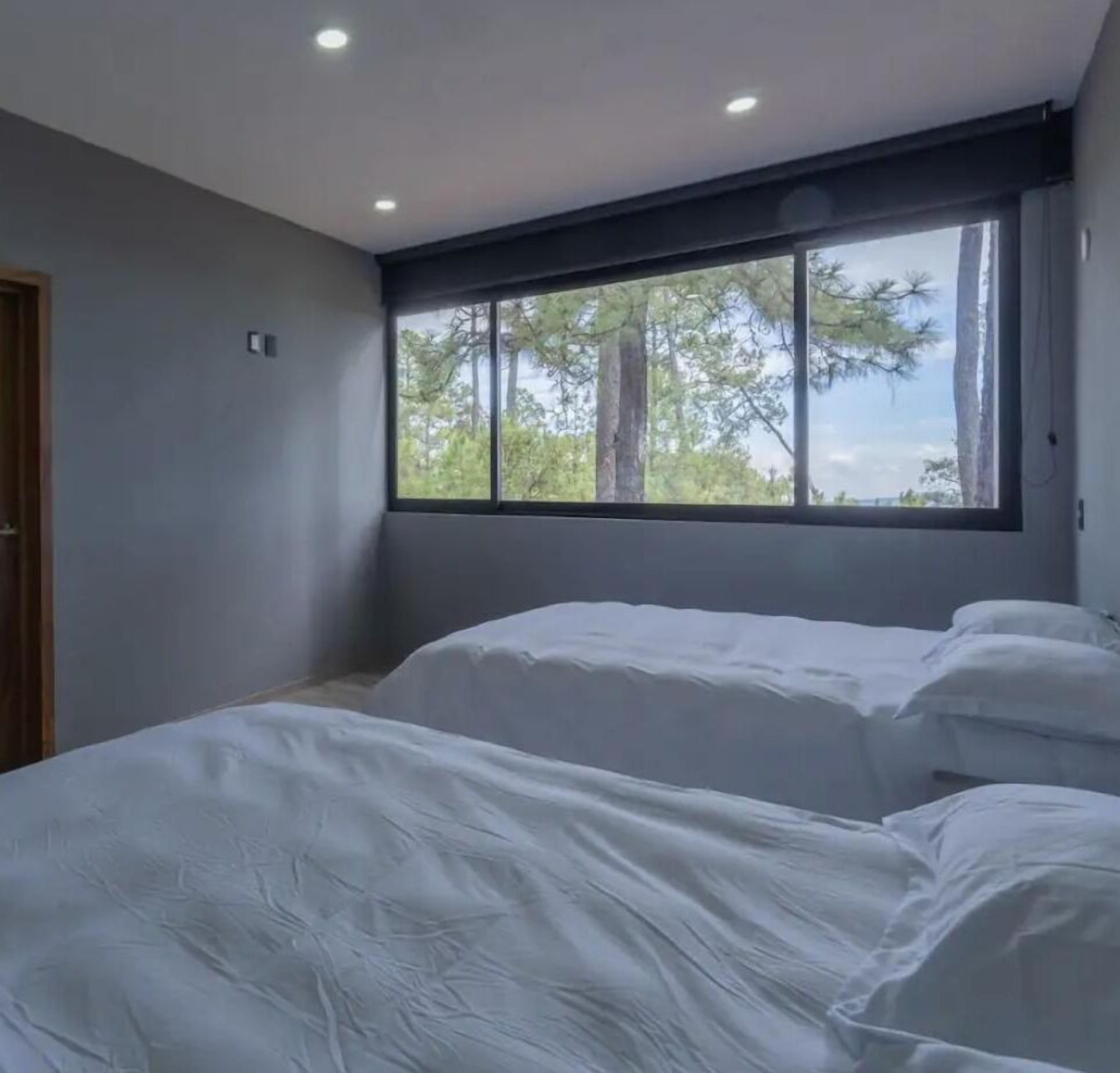 Quarto com uma janela grande, duas camas e uma porta.