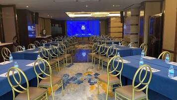 Sala de conferências com várias mesas e cadeiras, uma tela grande na frente e piso coberto de carpete.