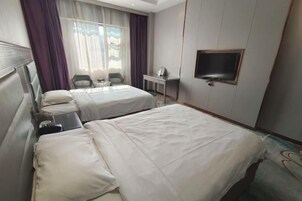 Quarto de hotel com duas camas, uma escrivaninha, uma cadeira e uma televisão.