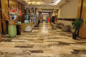 Um saguão de hotel com balcão de atendimento, área de estar e uma planta.