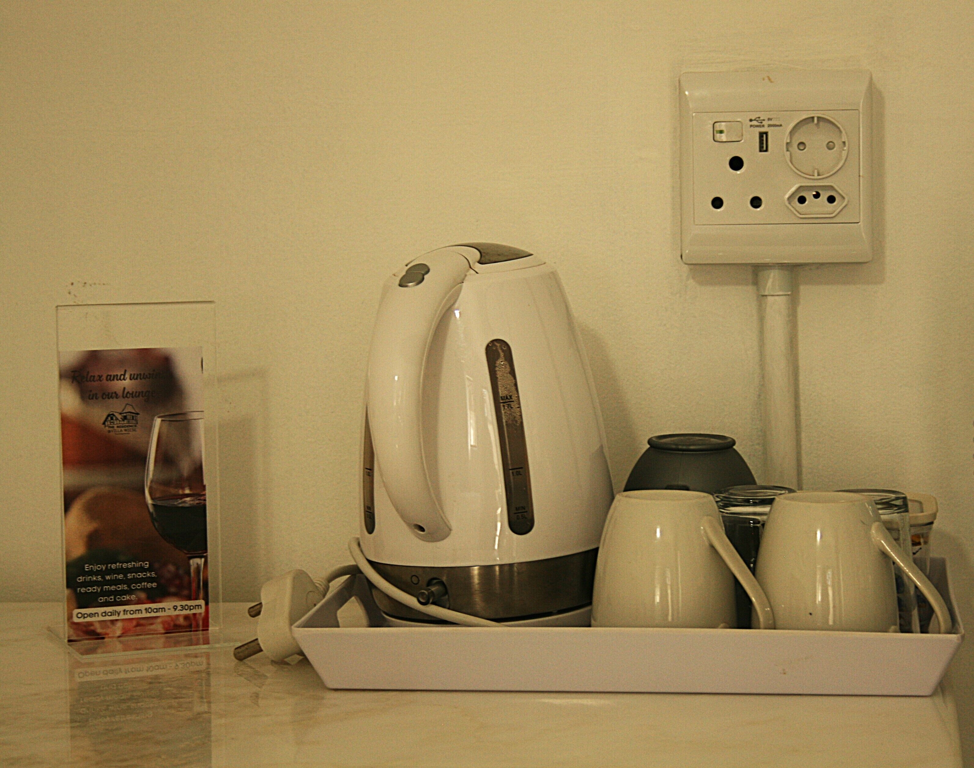 Uma área de cozinha com chaleira, cafeteira e um jarro de café em uma bancada.
